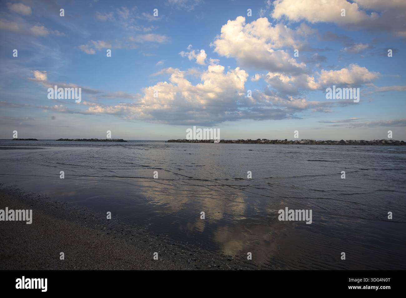 Beach by the seaside at sunset with a breakwater in the distance and a ...