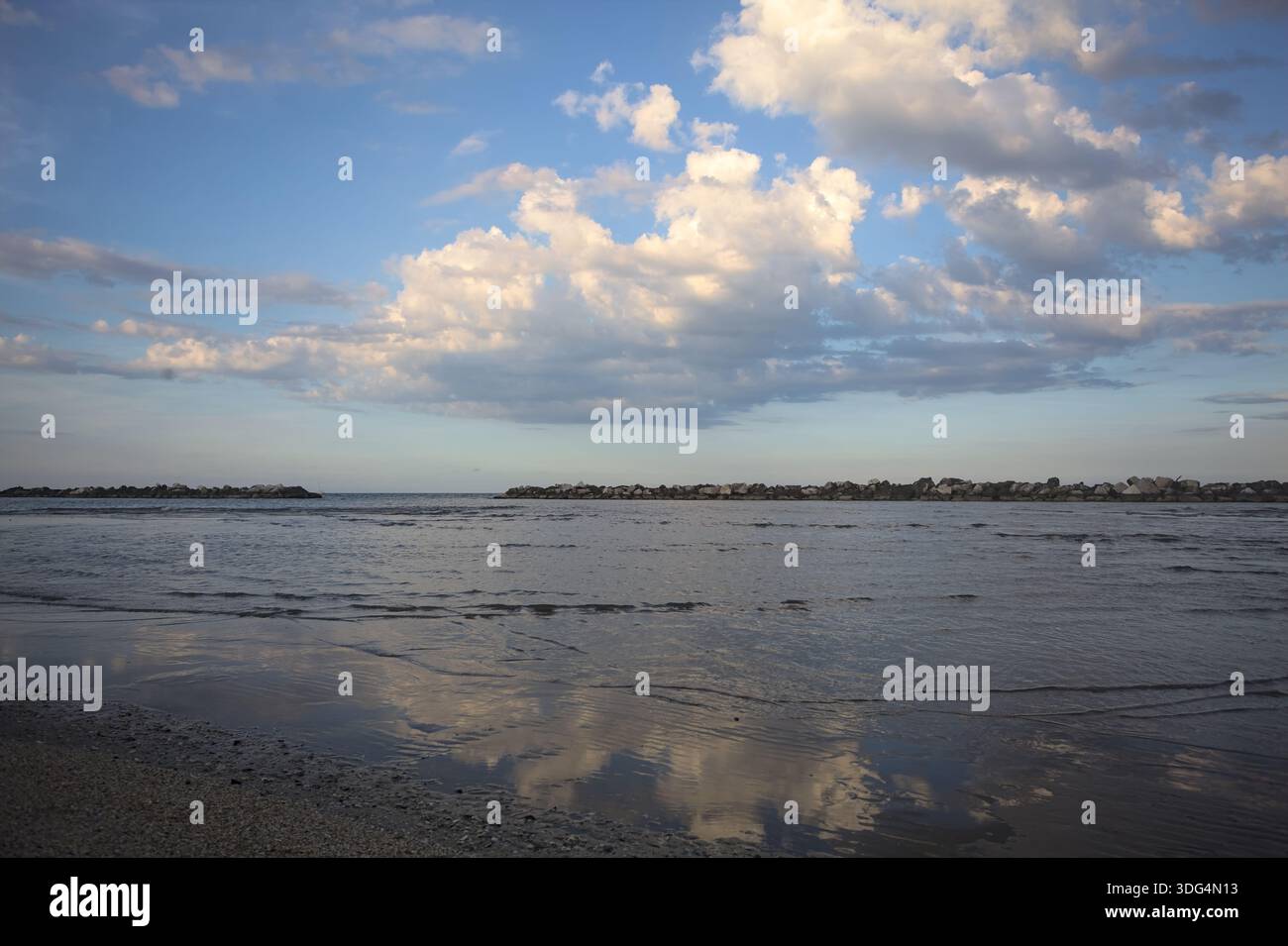 Beach by the seaside at sunset with a breakwater in the distance and a ...