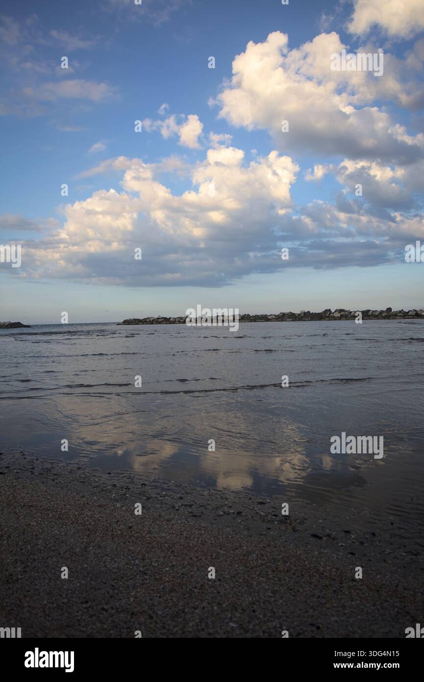Beach by the seaside at sunset with a breakwater in the distance and a ...