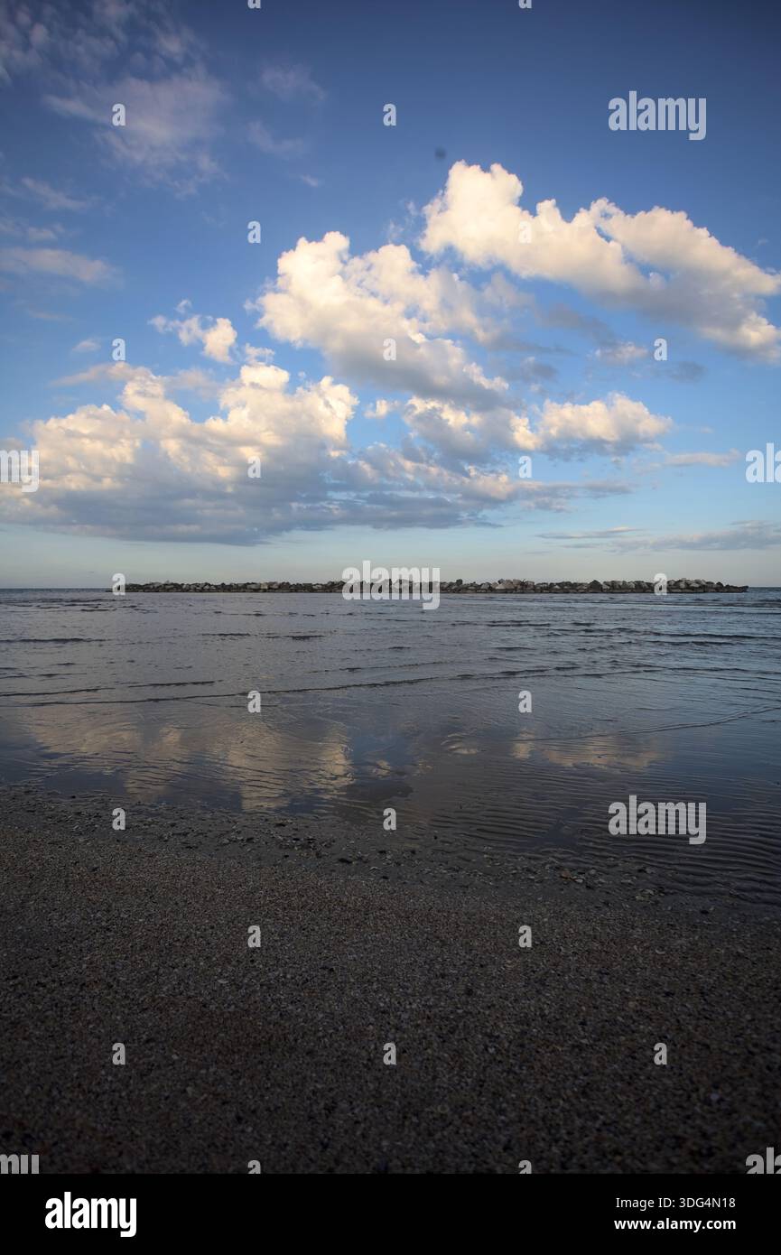 Beach by the seaside at sunset with a breakwater in the distance and a ...