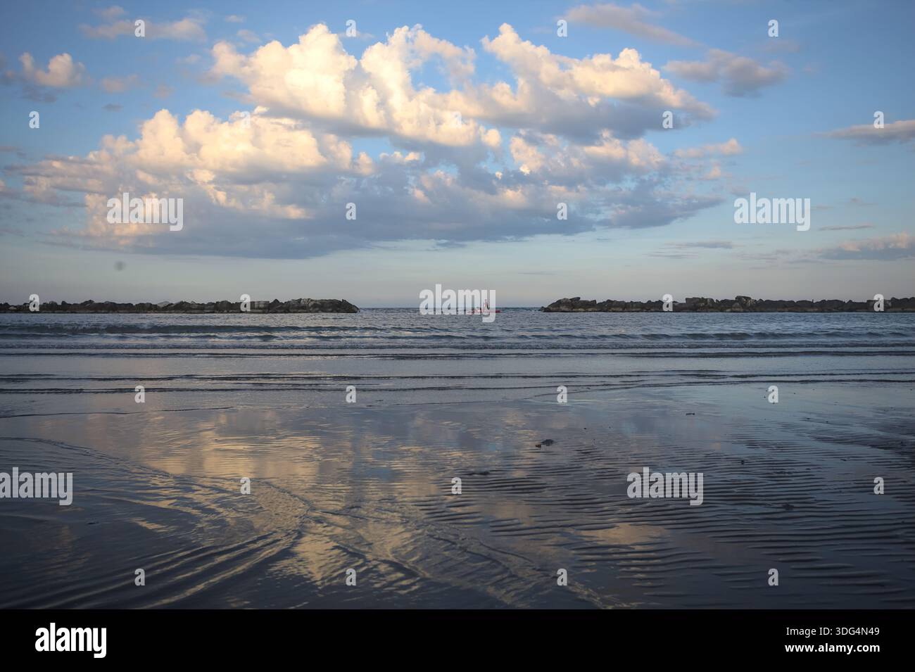 Beach by the seaside at sunset with a breakwater in the distance and a ...