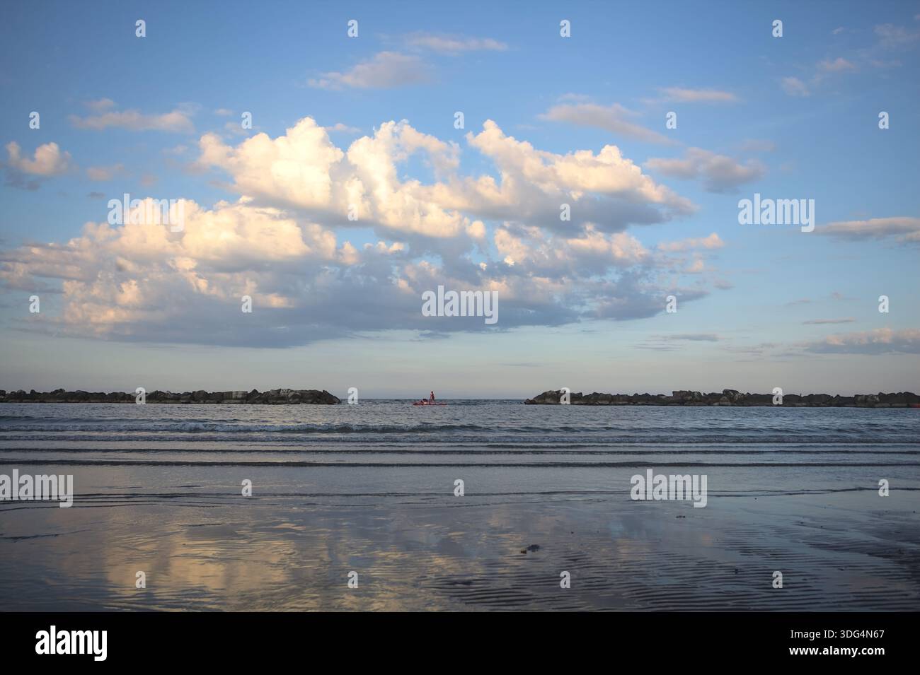 Beach by the seaside at sunset with a breakwater in the distance and a ...