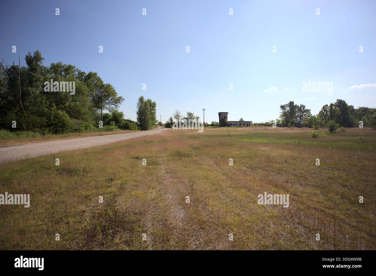 Dirt road blocked by a rusty bar next to a yard with dry grass and ...