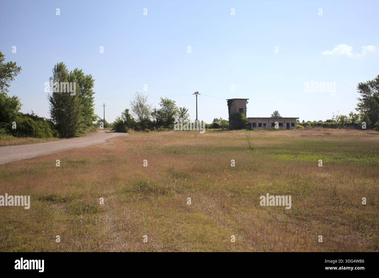 Dirt road blocked by a rusty bar next to a yard with dry grass and ...