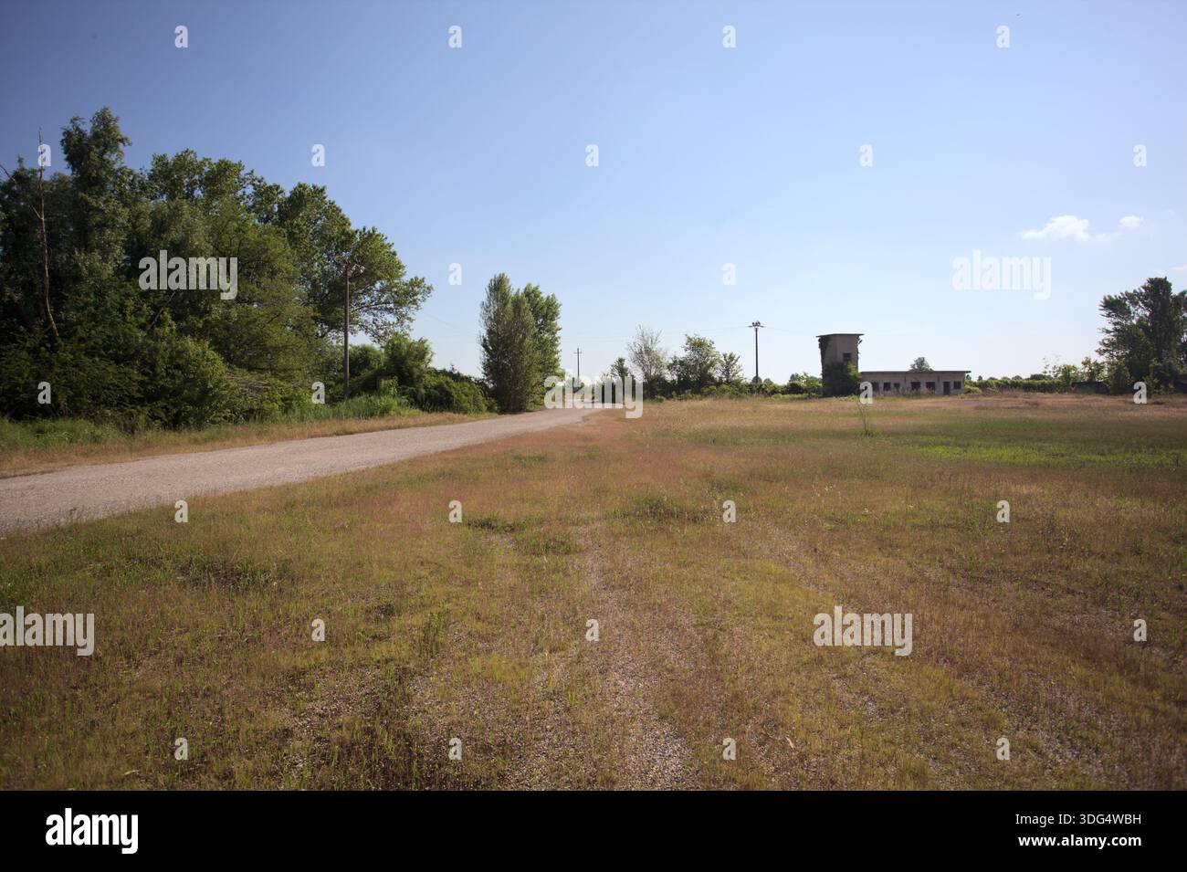 Dirt road blocked by a rusty bar next to a yard with dry grass and ...
