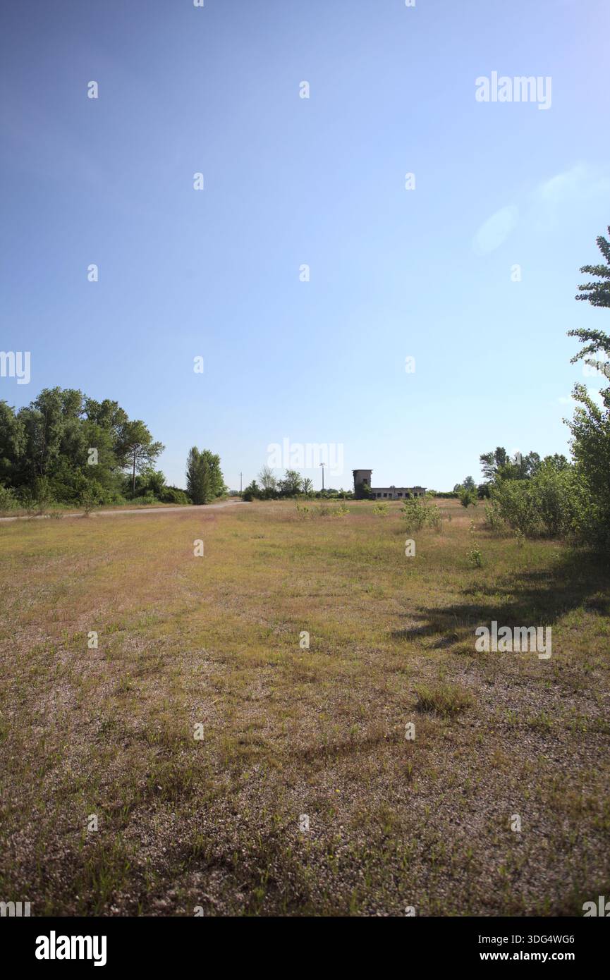 Dirt road blocked by a rusty bar next to a yard with dry grass and ...