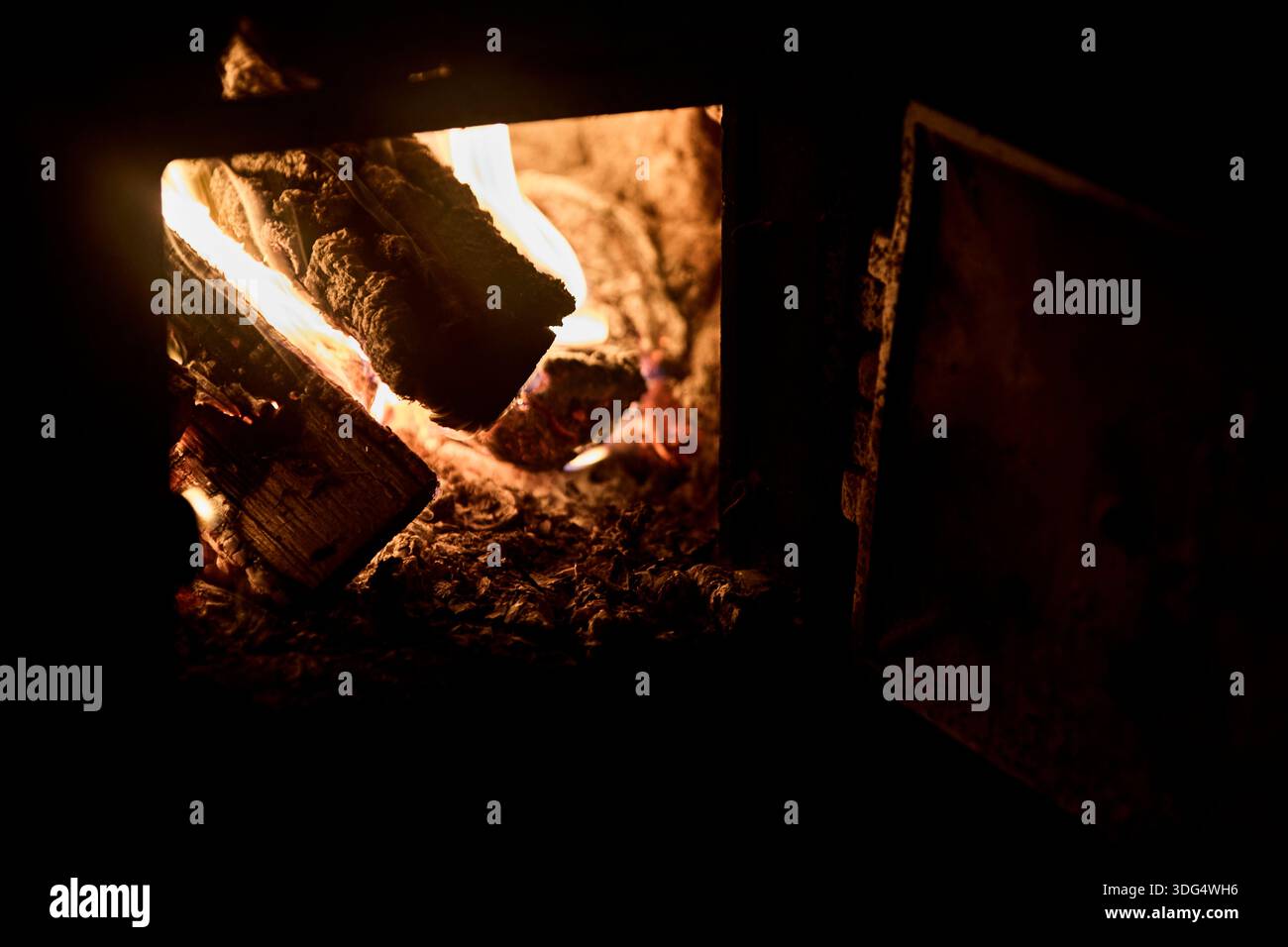 Close-up view of glowing coals and burning firewood inside an old stove ...