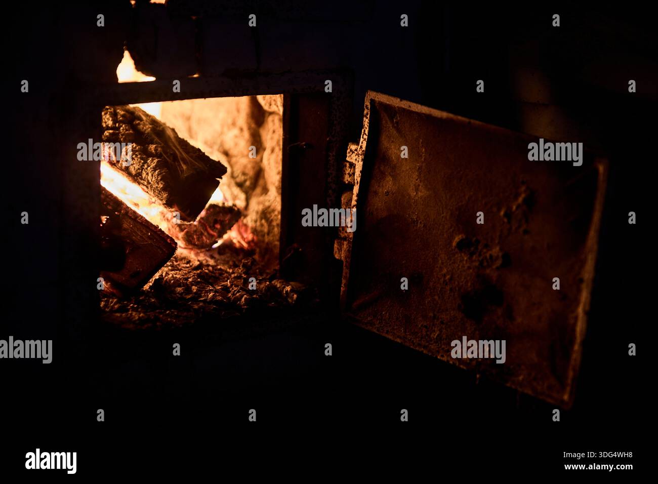 Close-up view of glowing coals and burning firewood inside an old stove ...