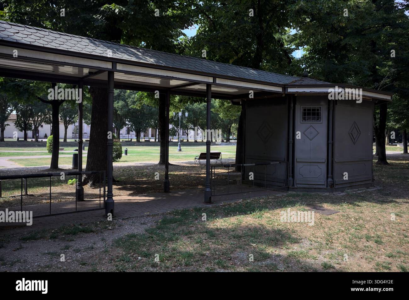 Closed kiosk in the shade under a few trees in a park on a sunny day ...