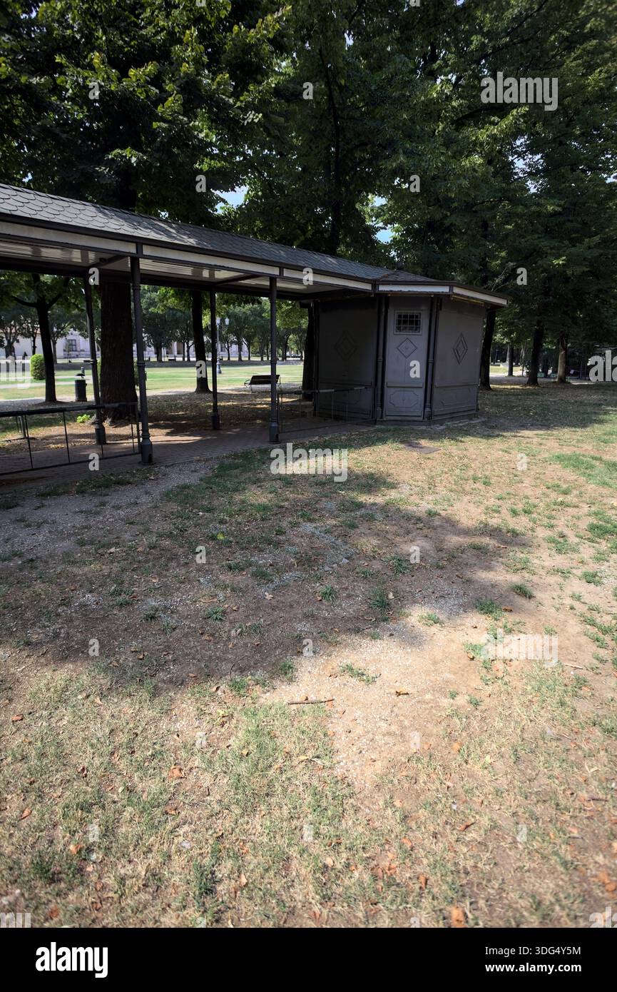 Closed kiosk in the shade under a few trees in a park on a sunny day ...