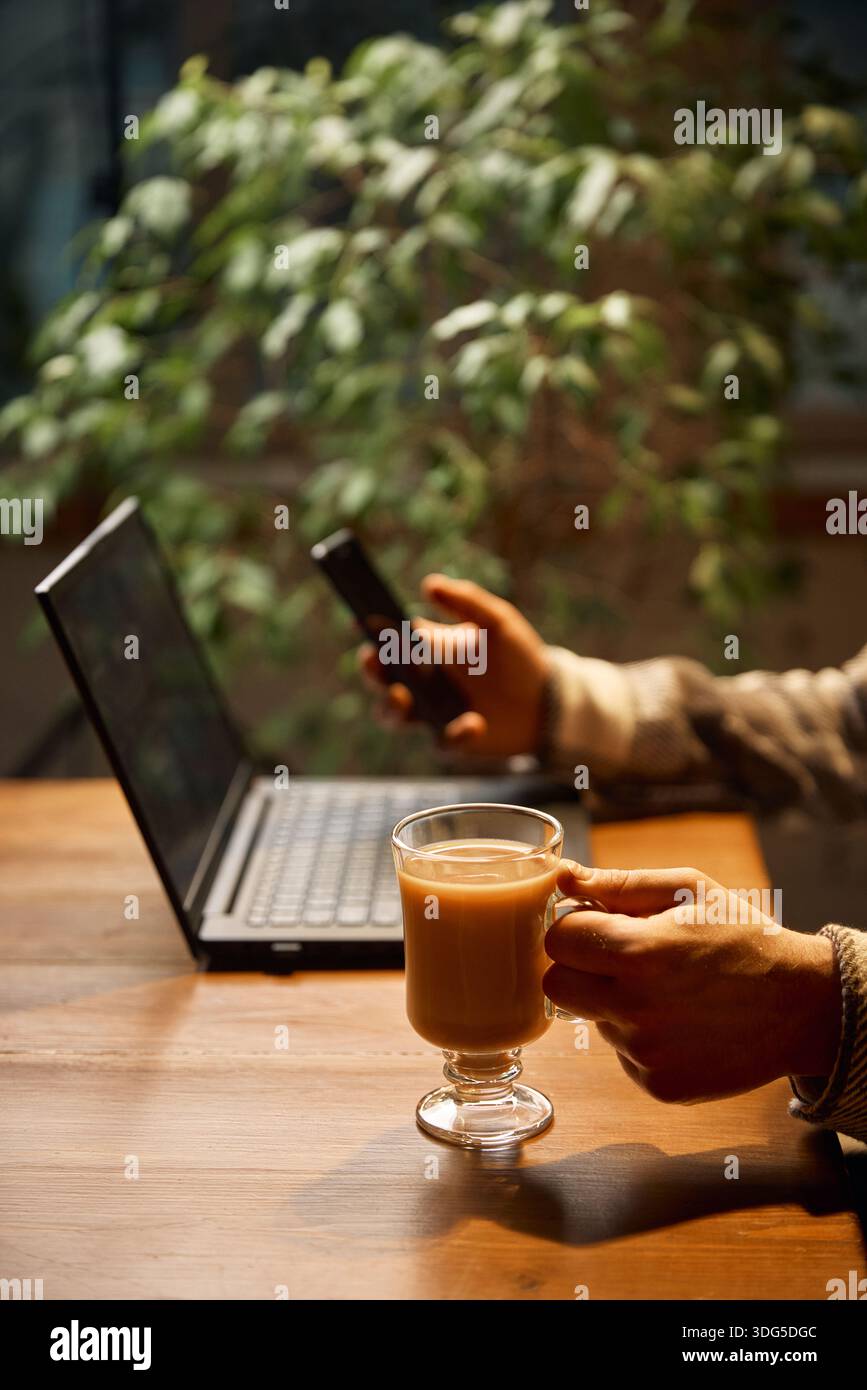 Hand holding glass latte cup with laptop and smartphone on table Stock ...