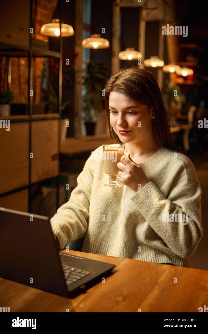 Woman drinking latte from glass cup while using laptop at cafe Stock ...