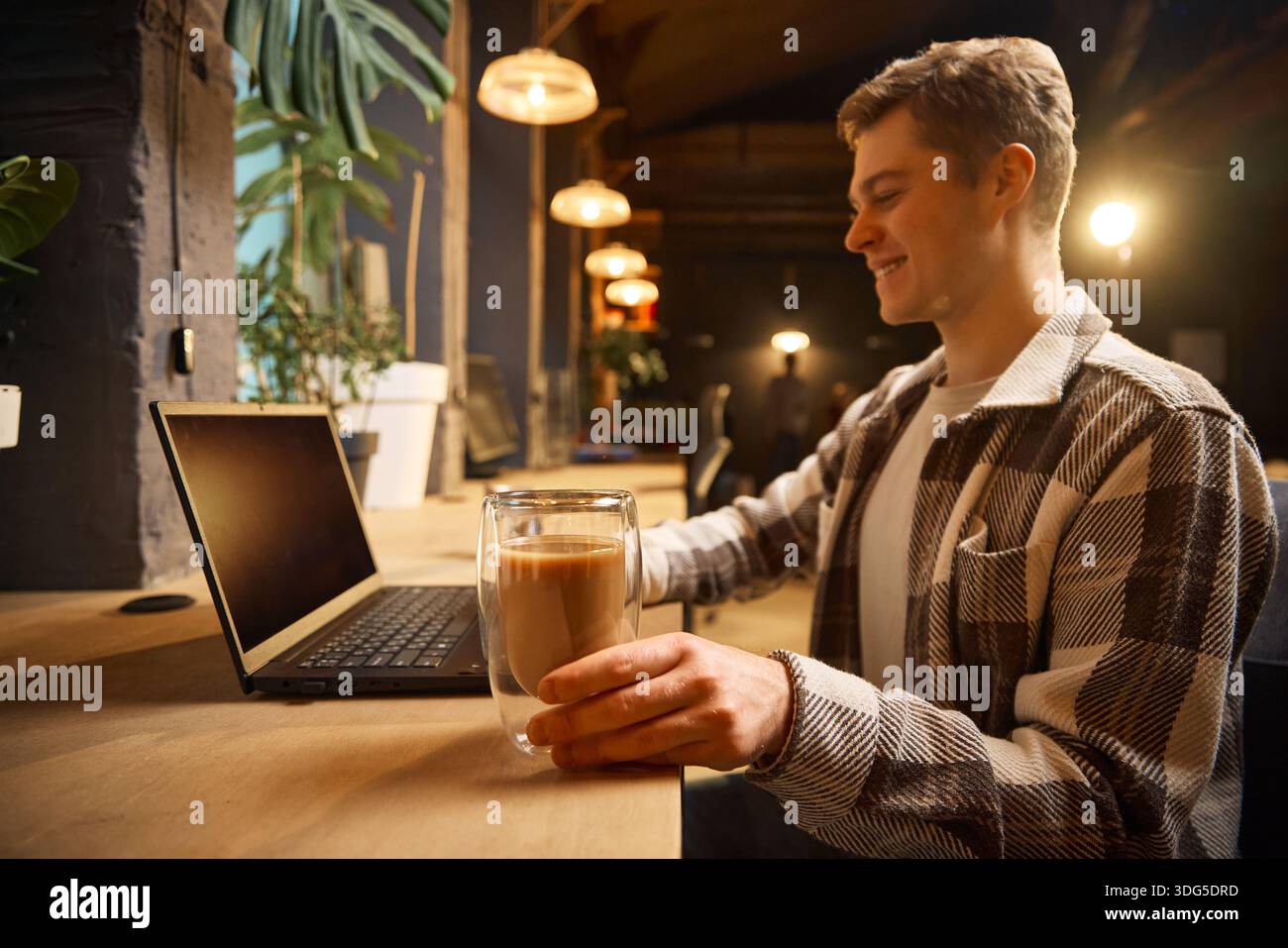 Young man working on laptop with glass of latte on wooden table in ...