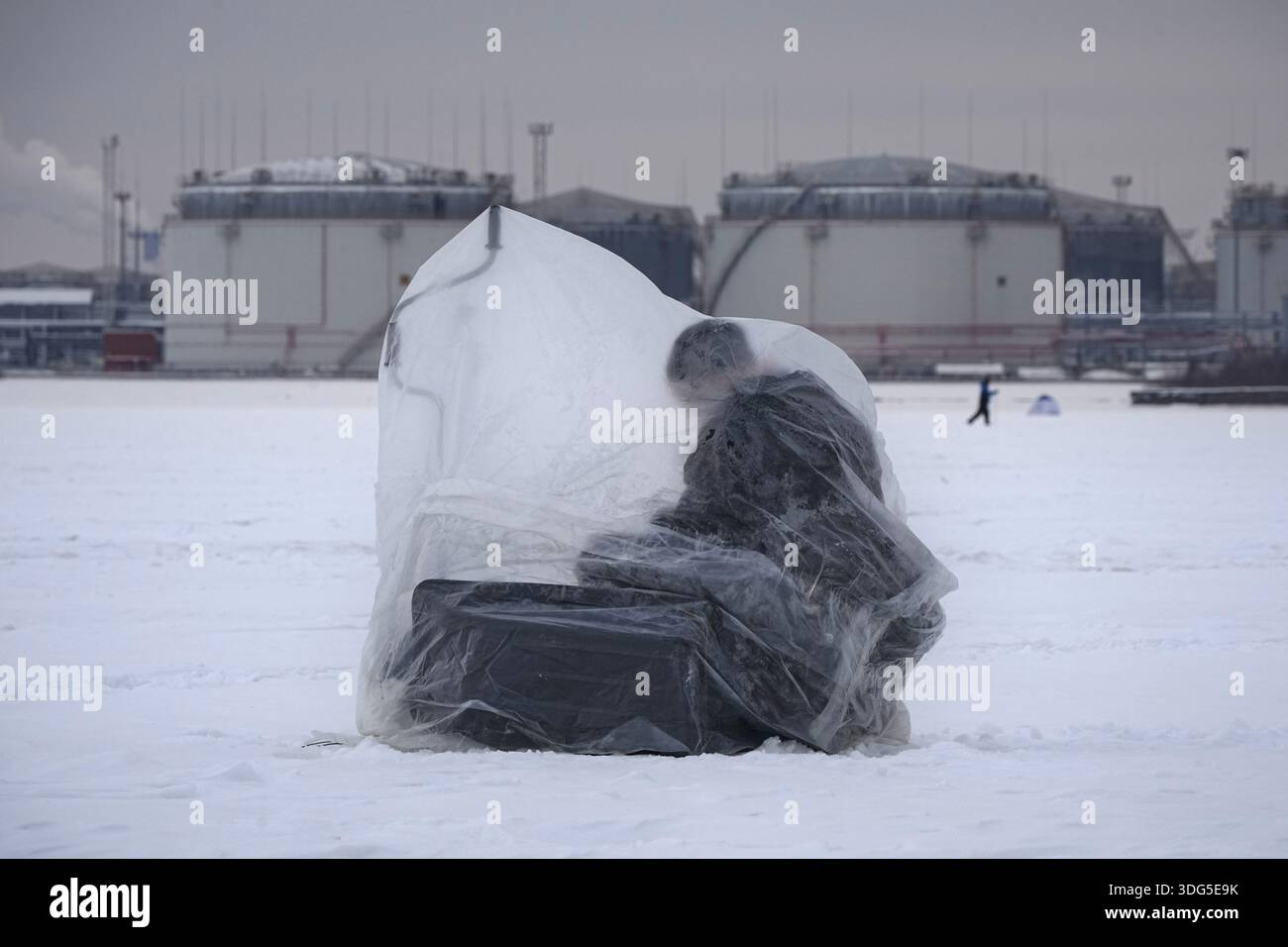A man fishes on the ice of the Gulf of Finland, sitting in a plastic ...