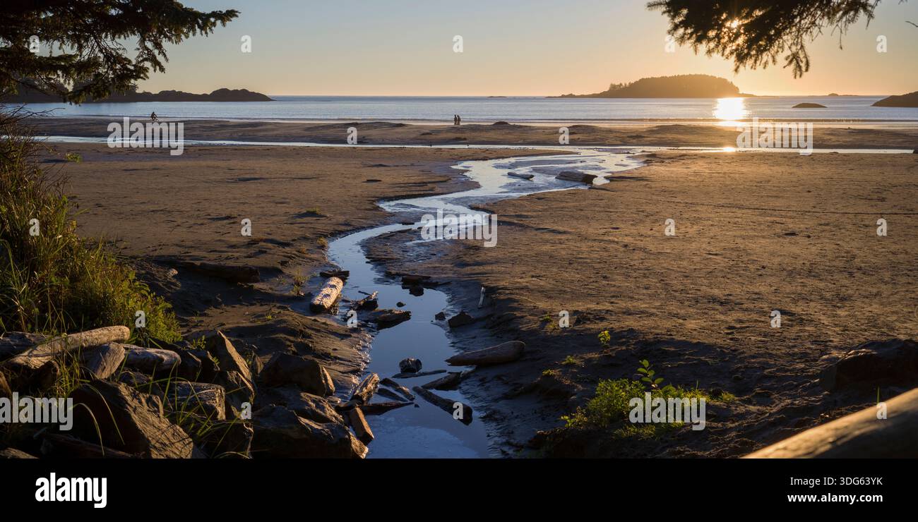 Sunset over a serene beach with a winding stream and distant islands ...