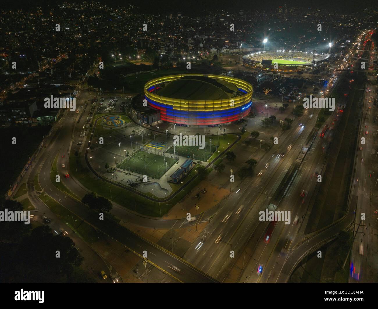 Night aerial view of a brightly lit stadium and bustling city traffic ...