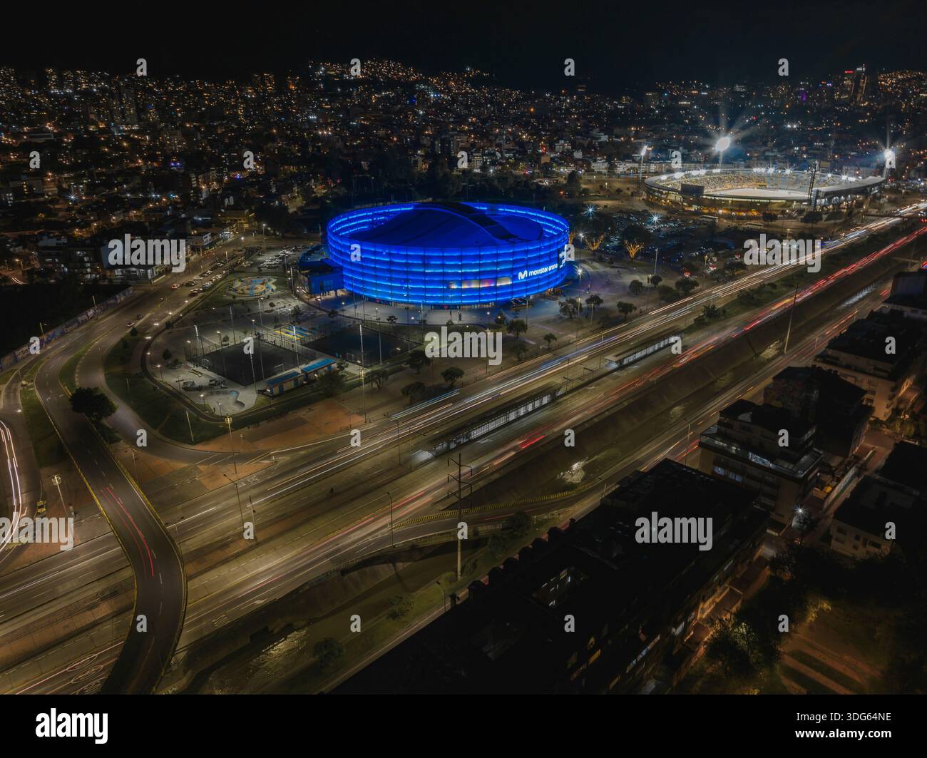 Illuminated blue stadium with city skyline and highway at night. Bogota ...