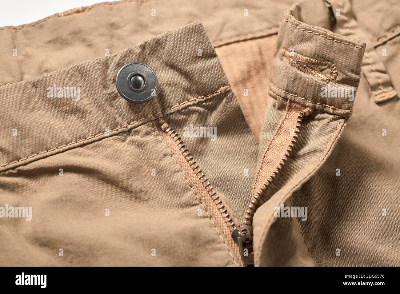 Close-up of beige pants, metal button and zipper partially unzipped ...