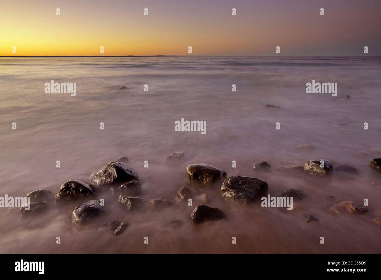 Tranquil seaside sunset with smooth waves and visible rocks in the ...