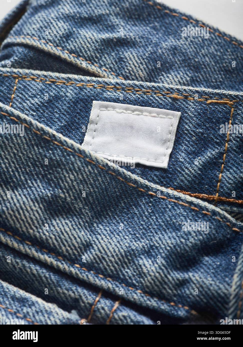 Close-up of folded blue denim jeans with a blank white label stitched ...