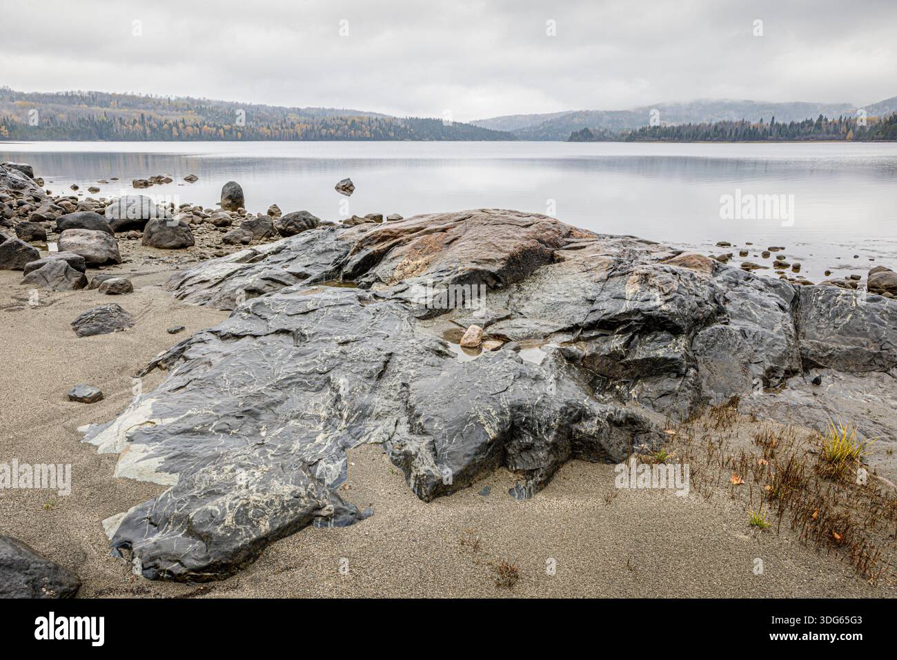 Rocky shoreline of a tranquil lake under grey skies with distant ...