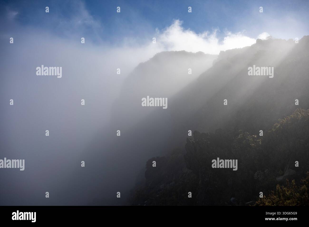 Misty mountain slope with sunlight breaking through clouds against a ...