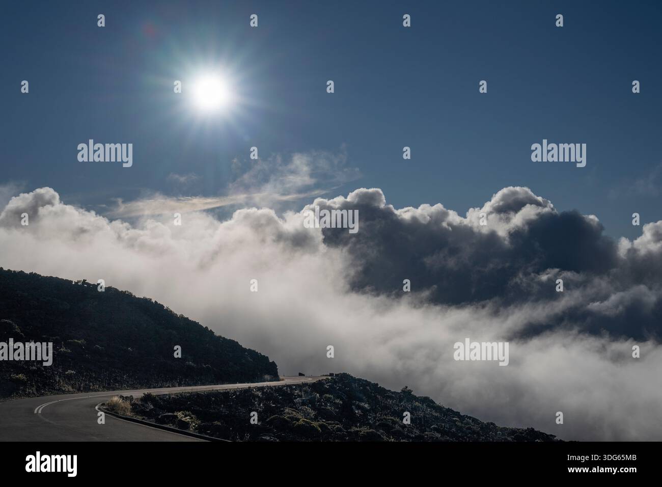 Bright sun shining over a winding mountain road surrounded by clouds ...