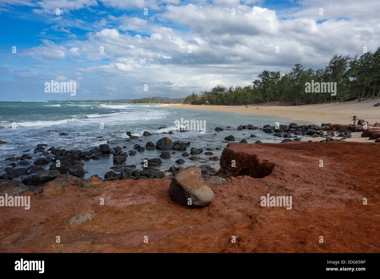 Rocky coastline with red earth, sandy beach and vibrant sky with clouds ...