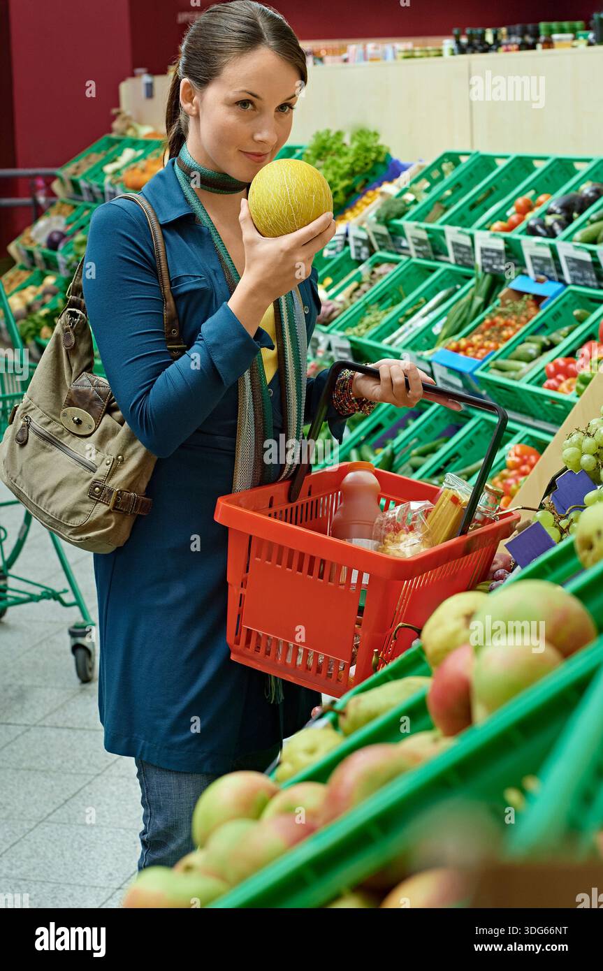 Woman smelling a melon in a grocery store produce section, holding a ...