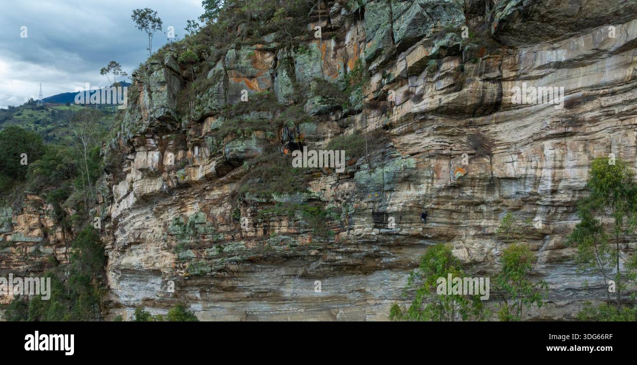 Rock climbers scaling a rugged cliff face with trees and cloudy sky in ...