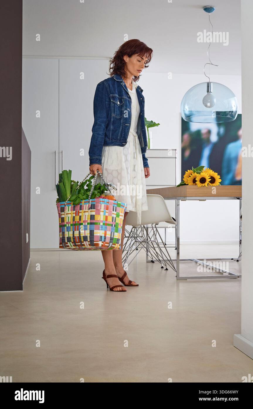 Woman in denim jacket carrying groceries in colorful basket in modern ...