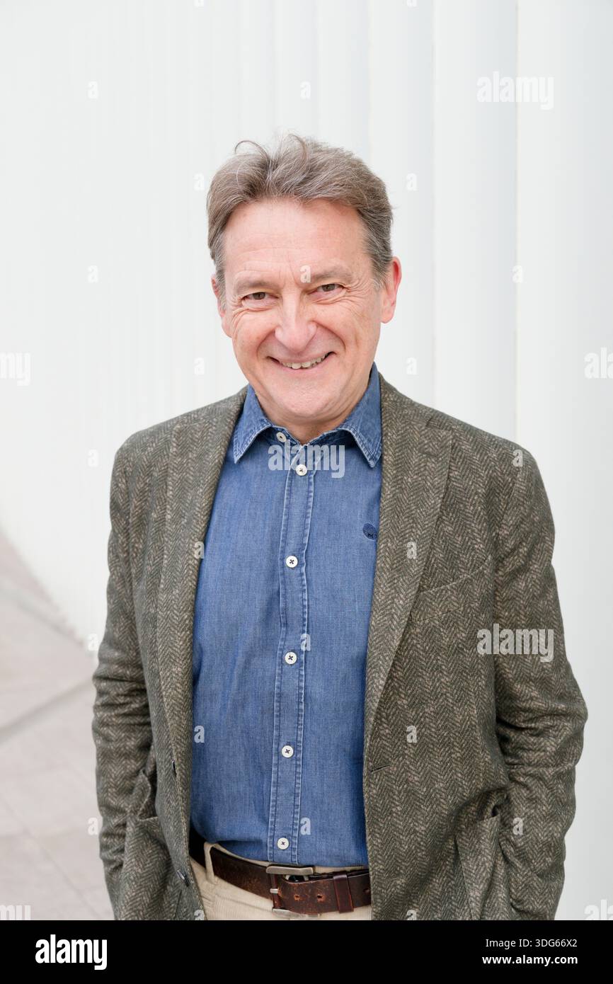 Smiling man in denim shirt and textured blazer against a white ...