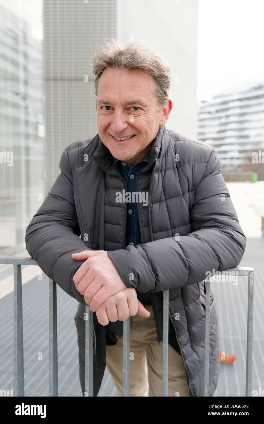Mature man in a puffer jacket leaning on a metal railing outdoors ...