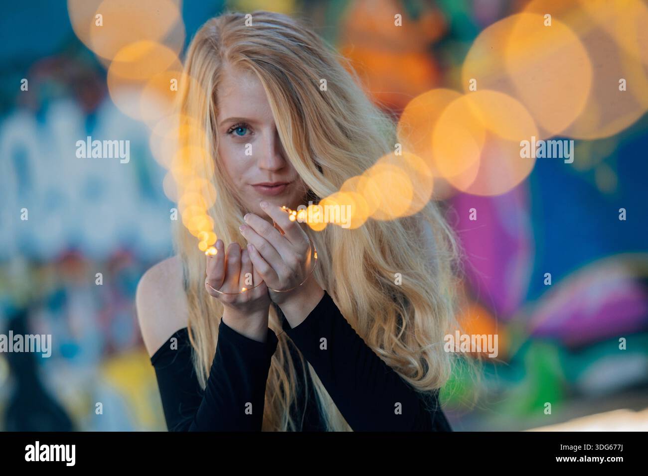 Young woman with long blonde hair holding string lights against ...