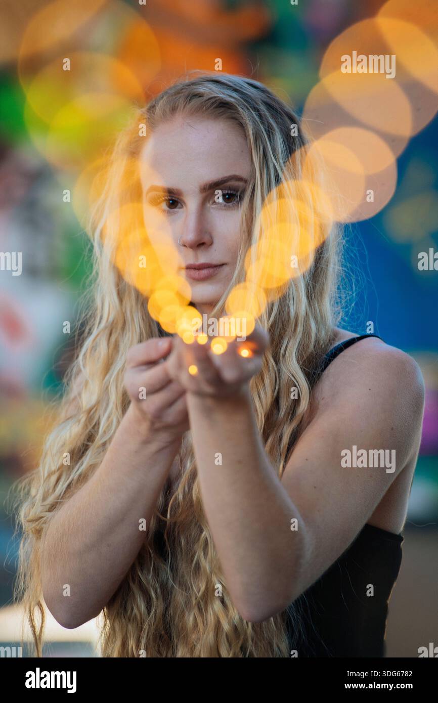 Woman with long blonde hair holds vibrant fairy lights in an artistic ...