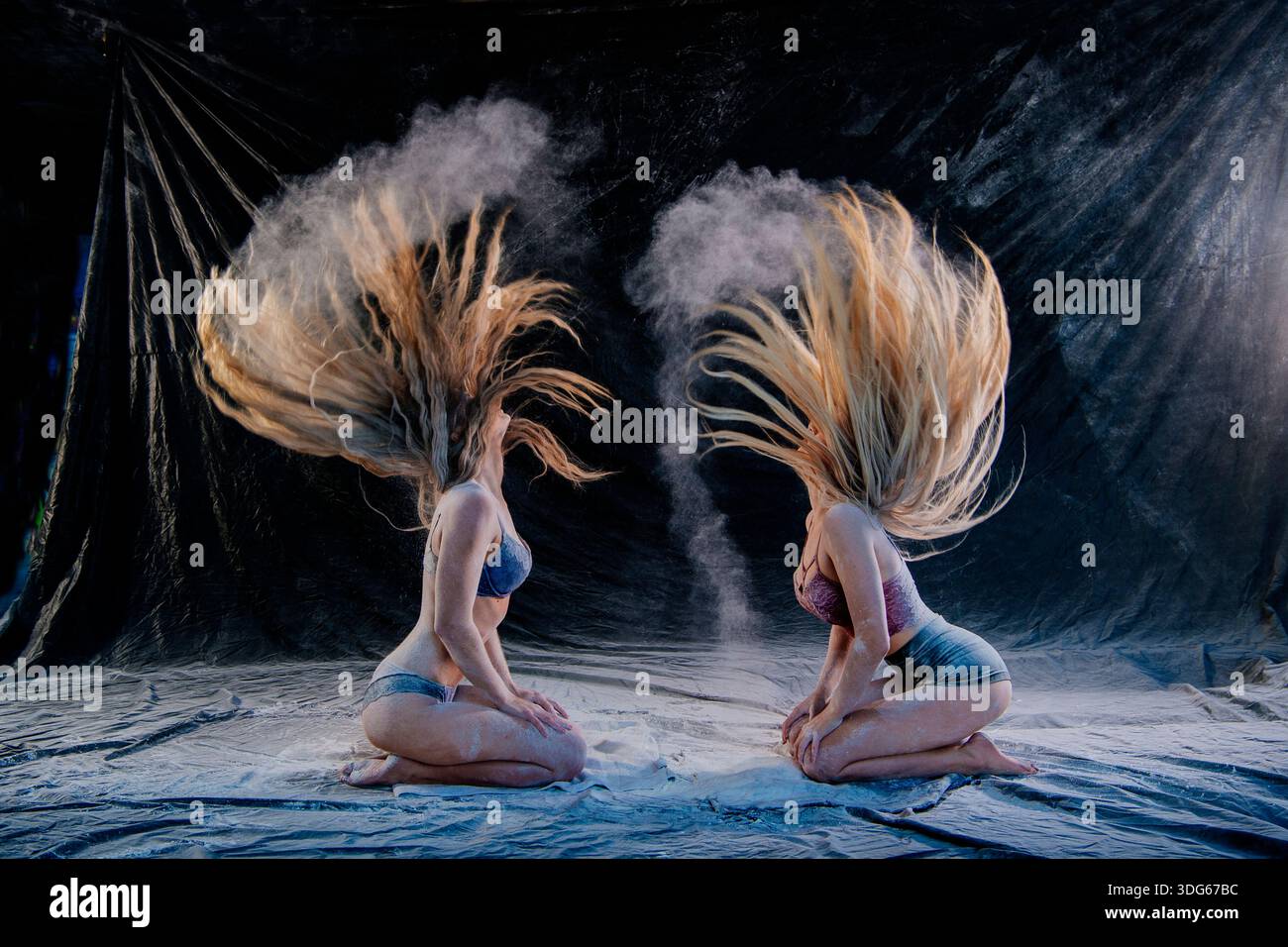 Two women kneel on fabric, flipping hair as powder creates dynamic ...