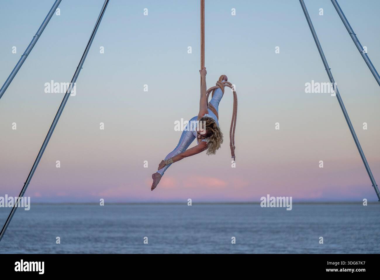 Aerial performer in silver outfit skillfully hangs on ropes over the ...