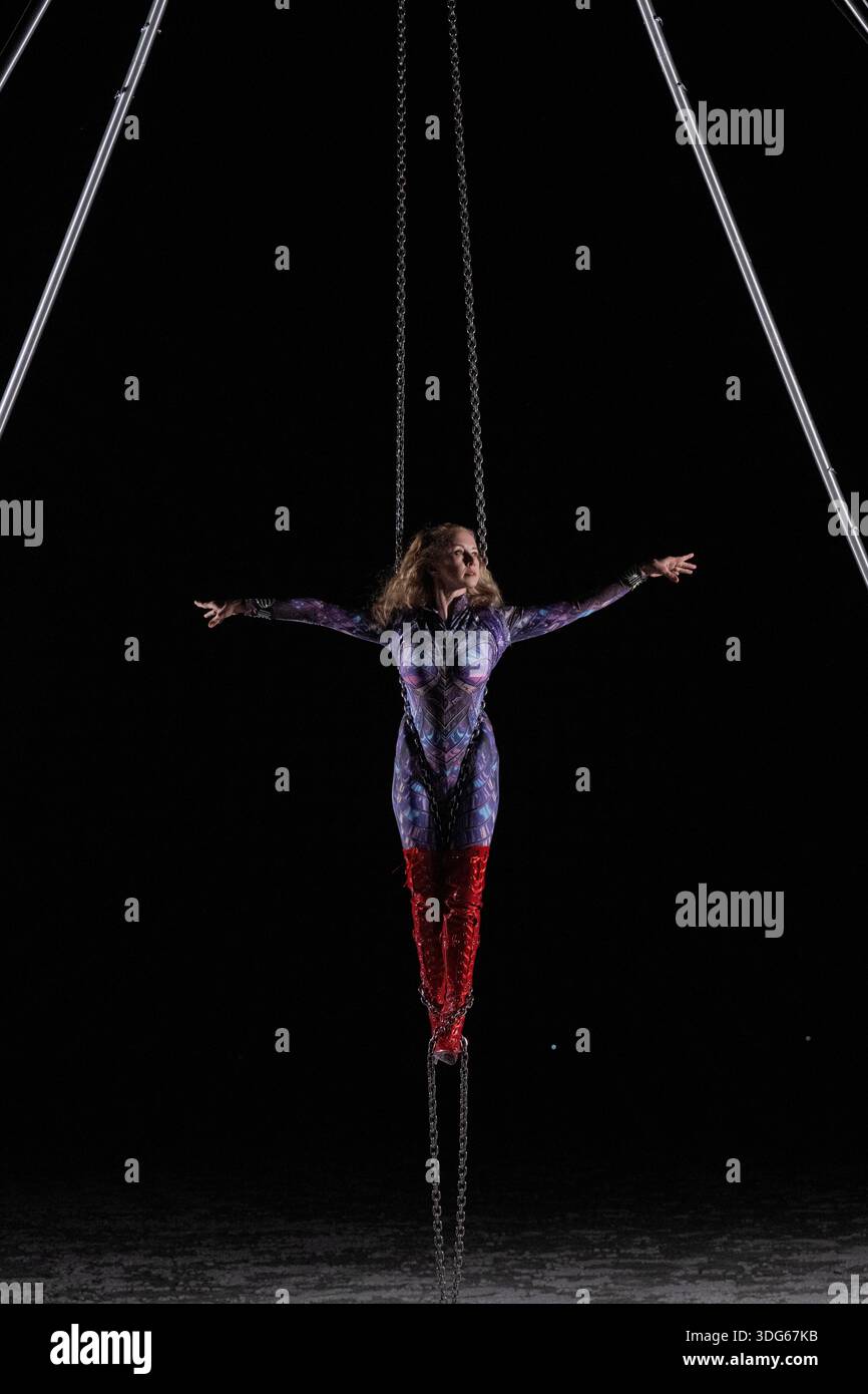 Aerial artist performing on chains in a dark, dramatic setting, wearing ...