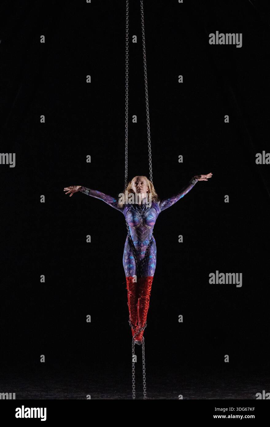 Aerial acrobat performs suspended in chains wearing a colorful bodysuit ...