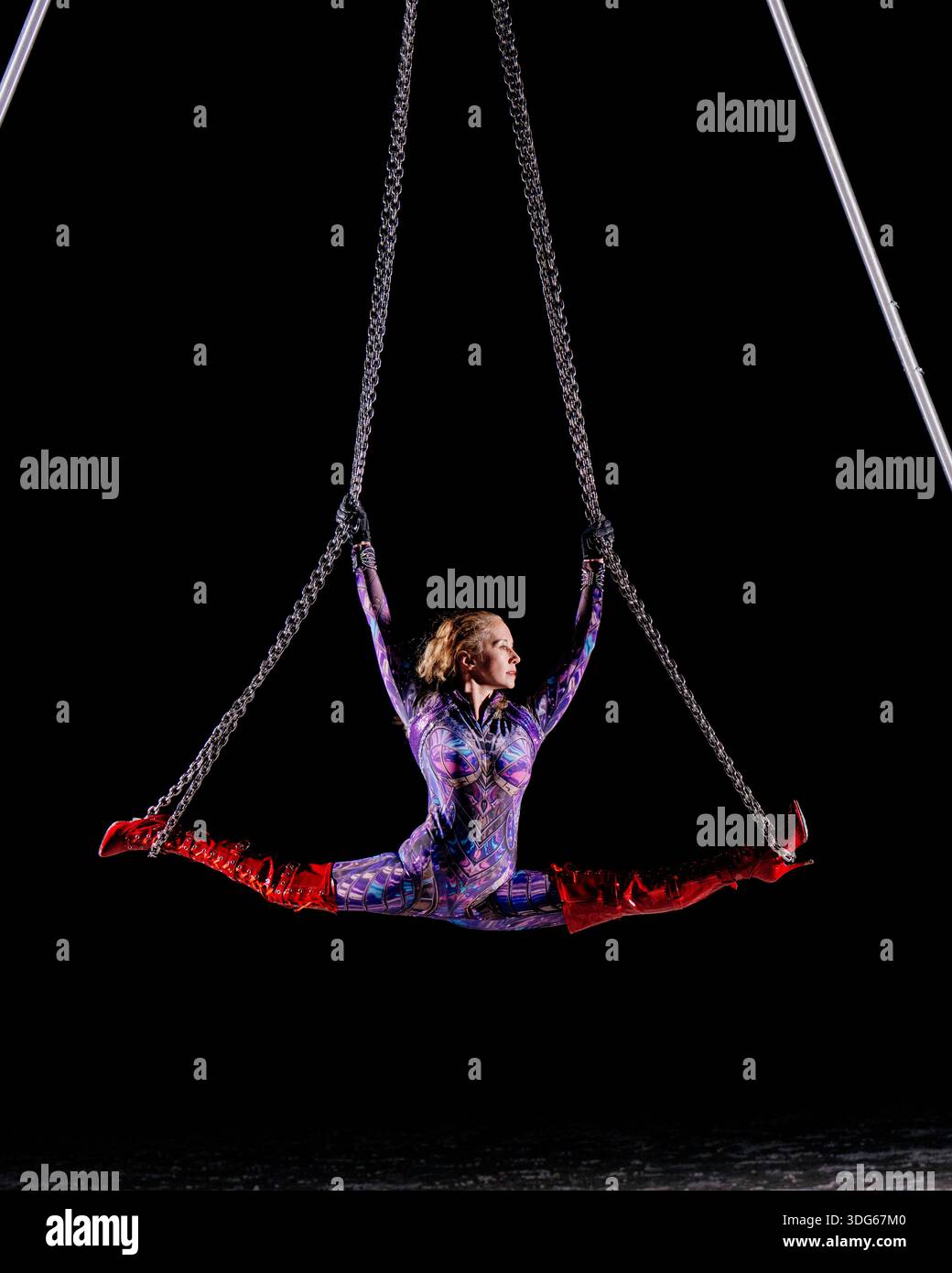 Aerial performer doing splits on chains in dramatic lighting with red ...
