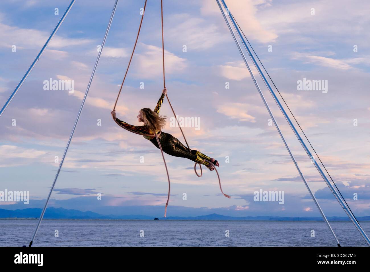 Aerial performer in colorful suit gracefully swings over a calm sea at ...