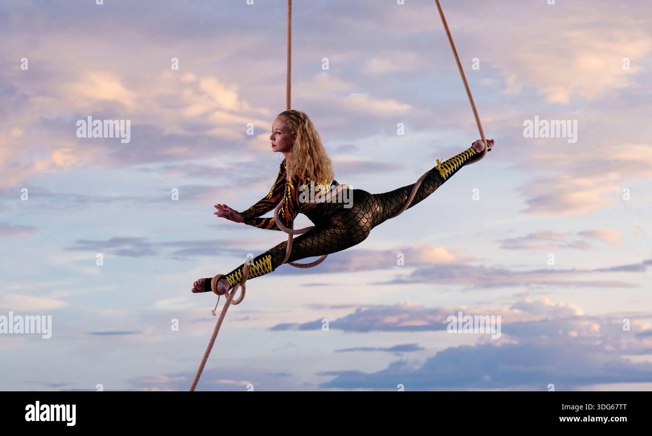 Aerial performer in split position on ropes against a dramatic sky ...