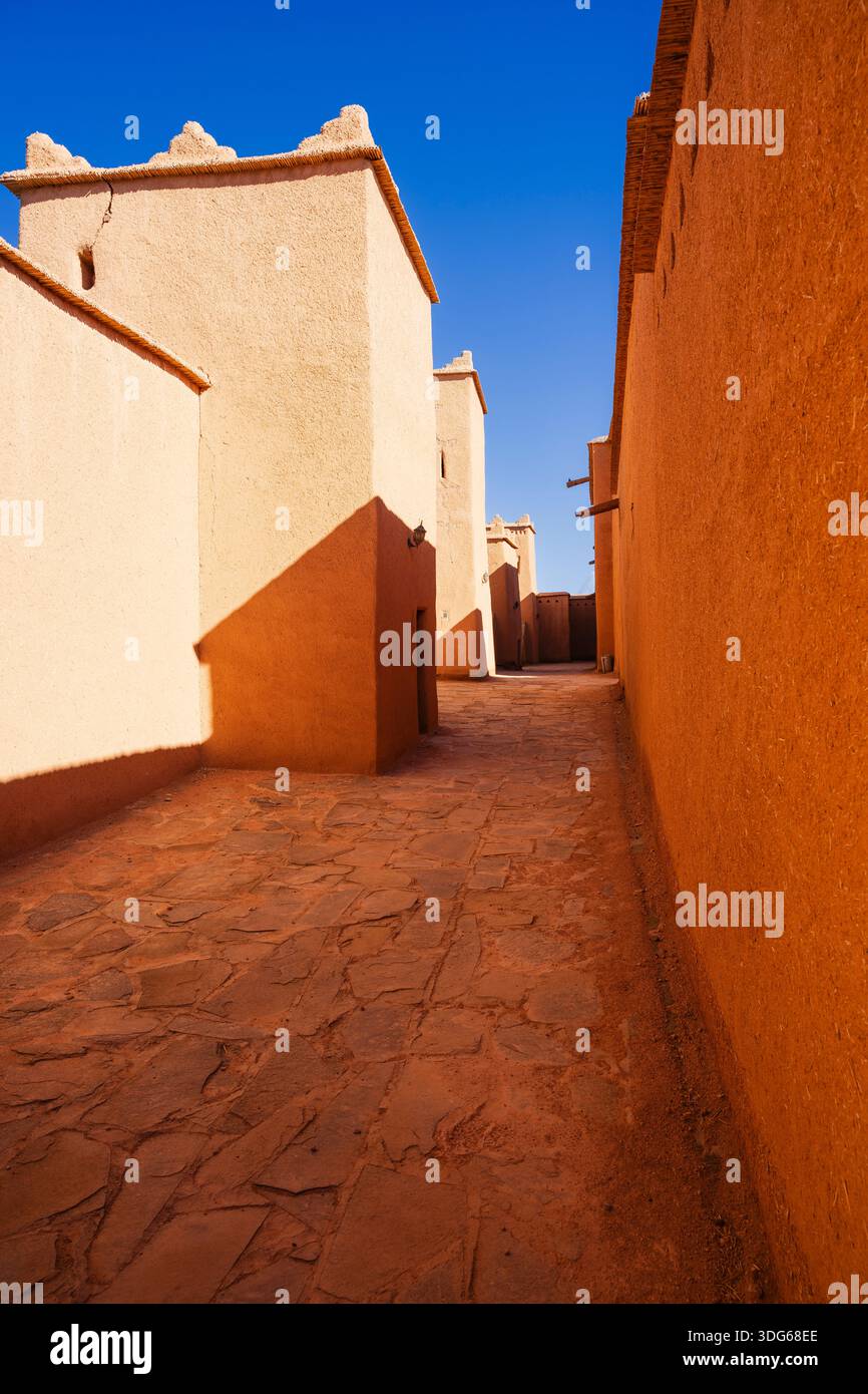 Narrow alley with earthen walls and bright blue sky in a traditional ...
