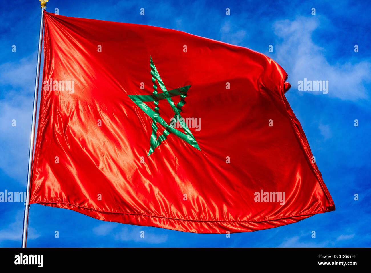 Bright red Moroccan flag with green star on a clear blue sky background ...