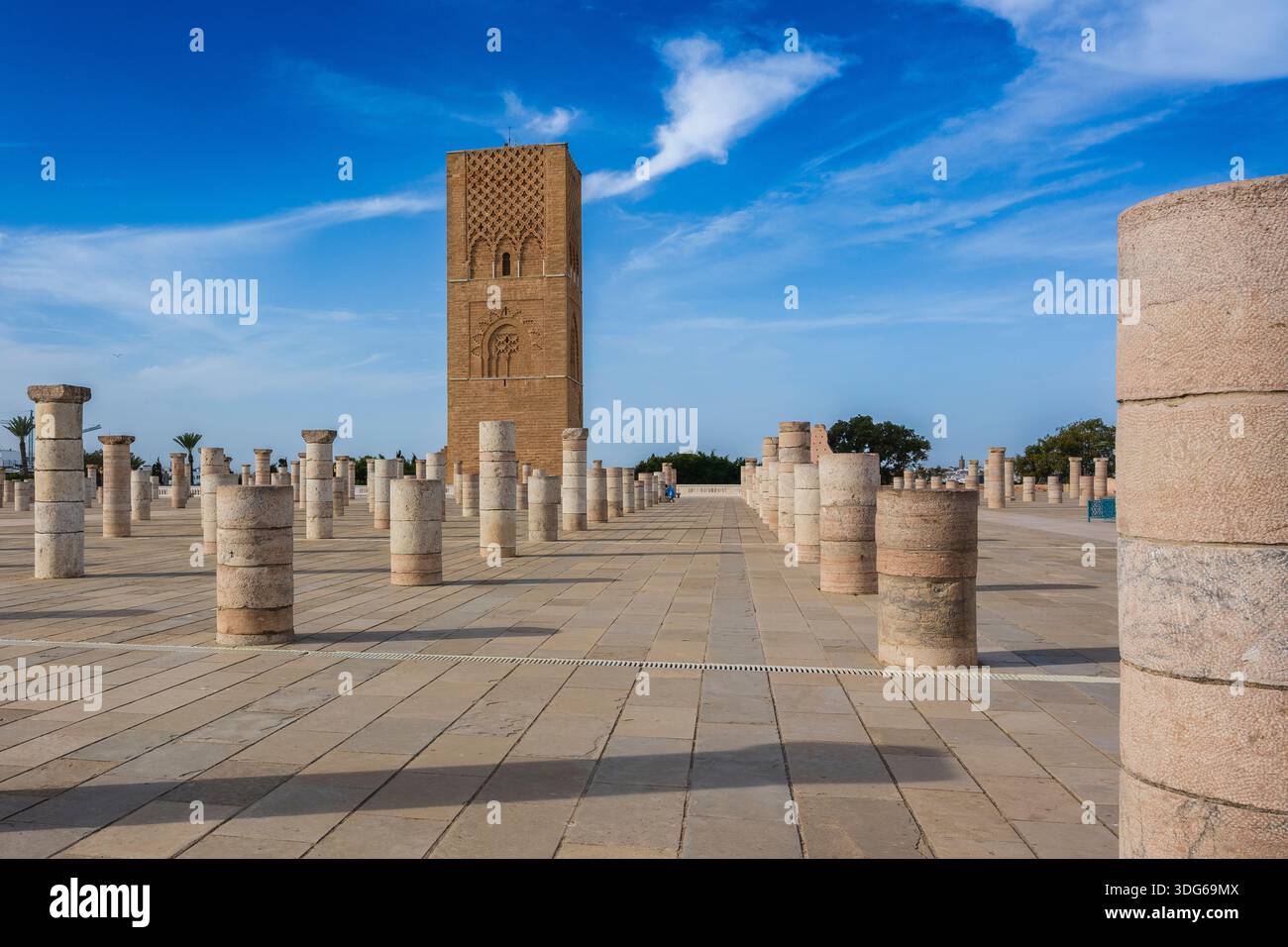 Ancient stone columns surround the Hassan Tower under a bright blue sky ...
