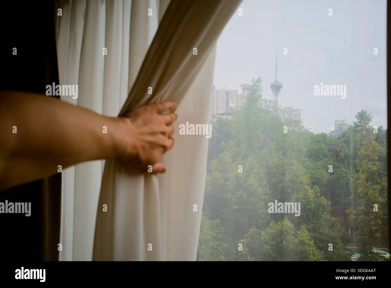 Hand opening curtain to reveal cityscape with tower and lush green ...