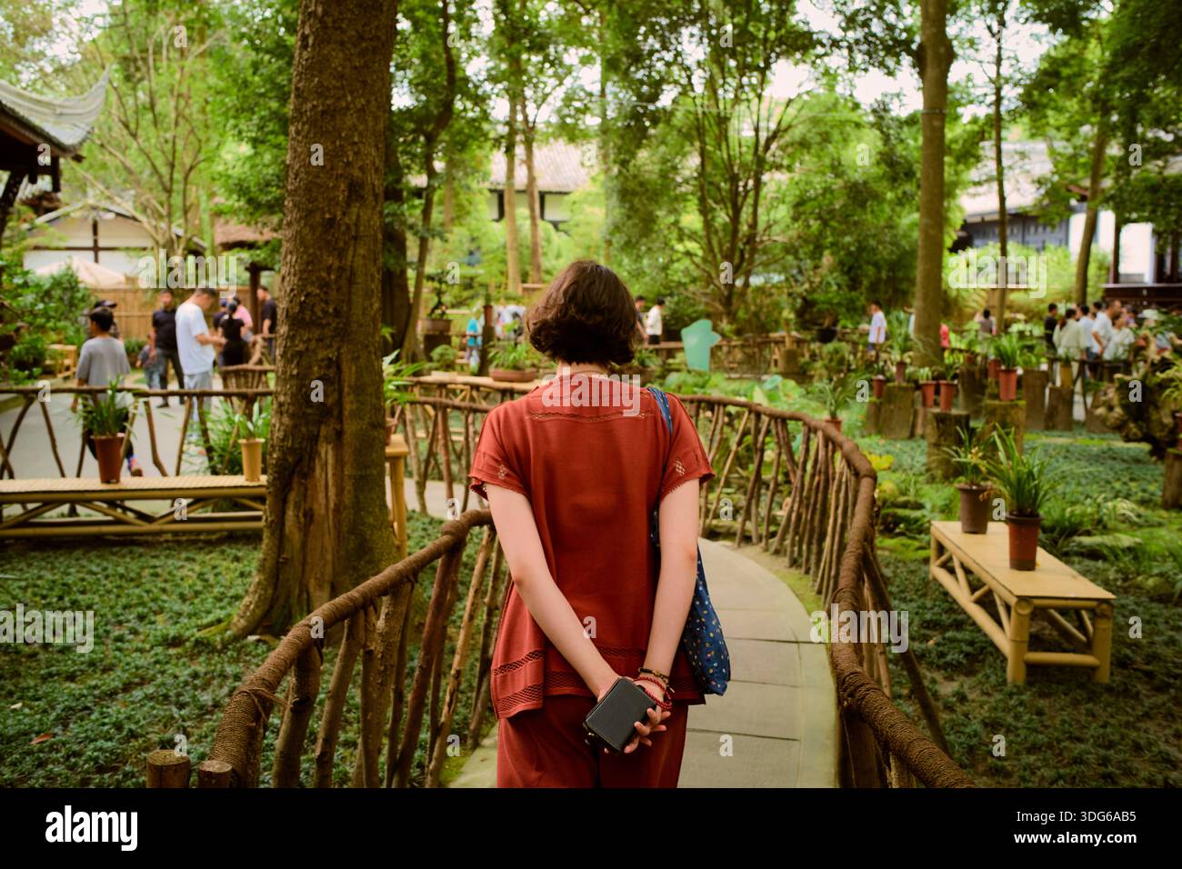 A person in red clothing walks down a tree-lined path in a lush garden ...