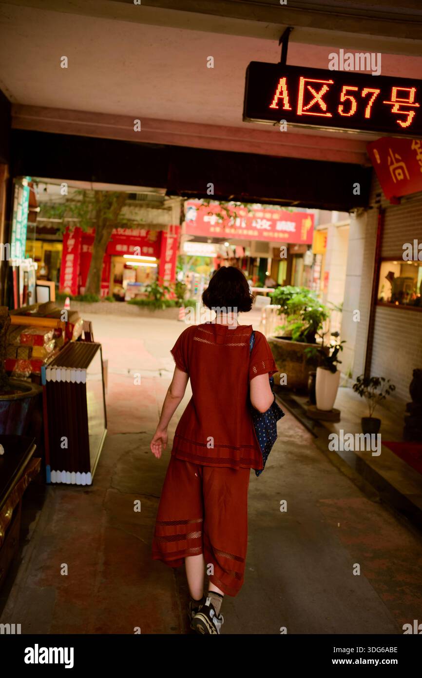 Woman in red outfit walks through market alley during the day carrying ...