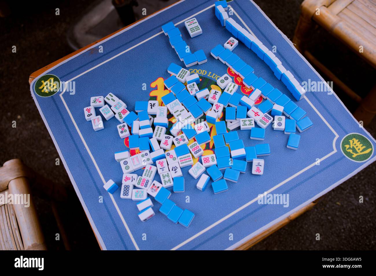 Mahjong tiles scattered on a blue table surrounded by bamboo chairs ...