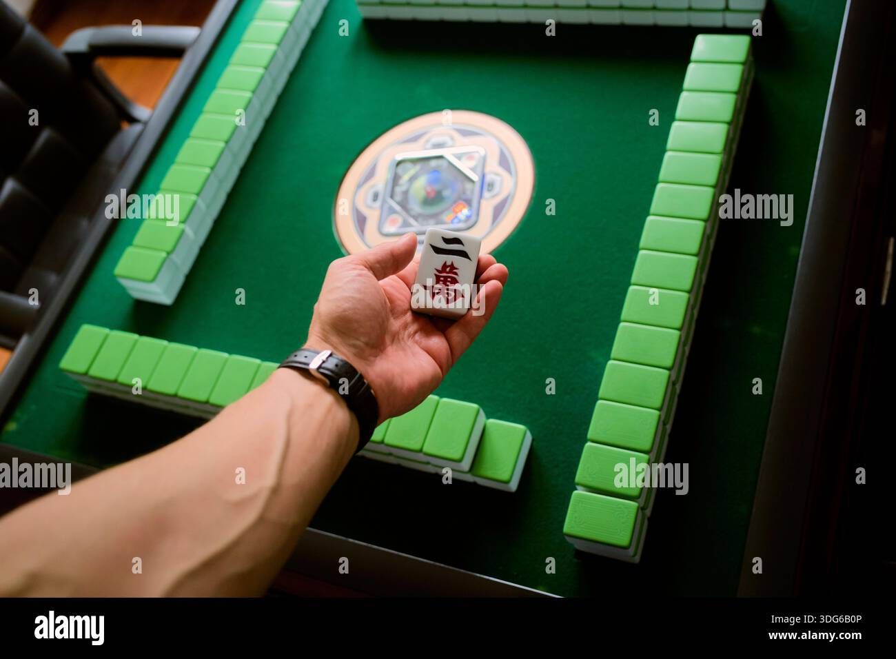 Hand holding a Mahjong tile with a green game table setup in the ...